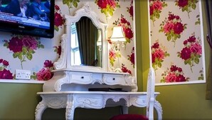 Quarto com toucador branco, espelho e papel de parede floral.