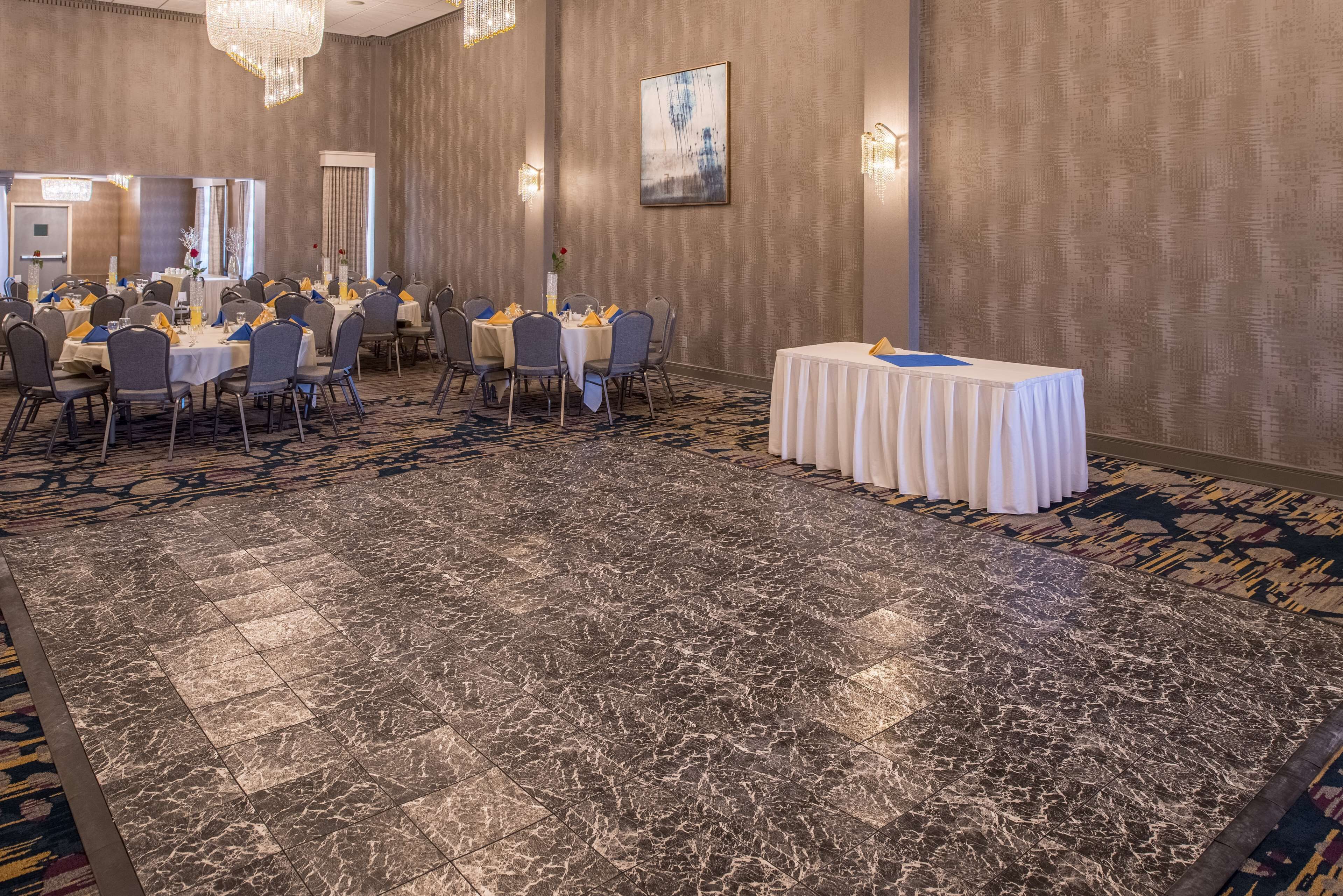 Sala de conferência com mesas redondas, cadeiras e uma mesa branca com um jogo americano azul.