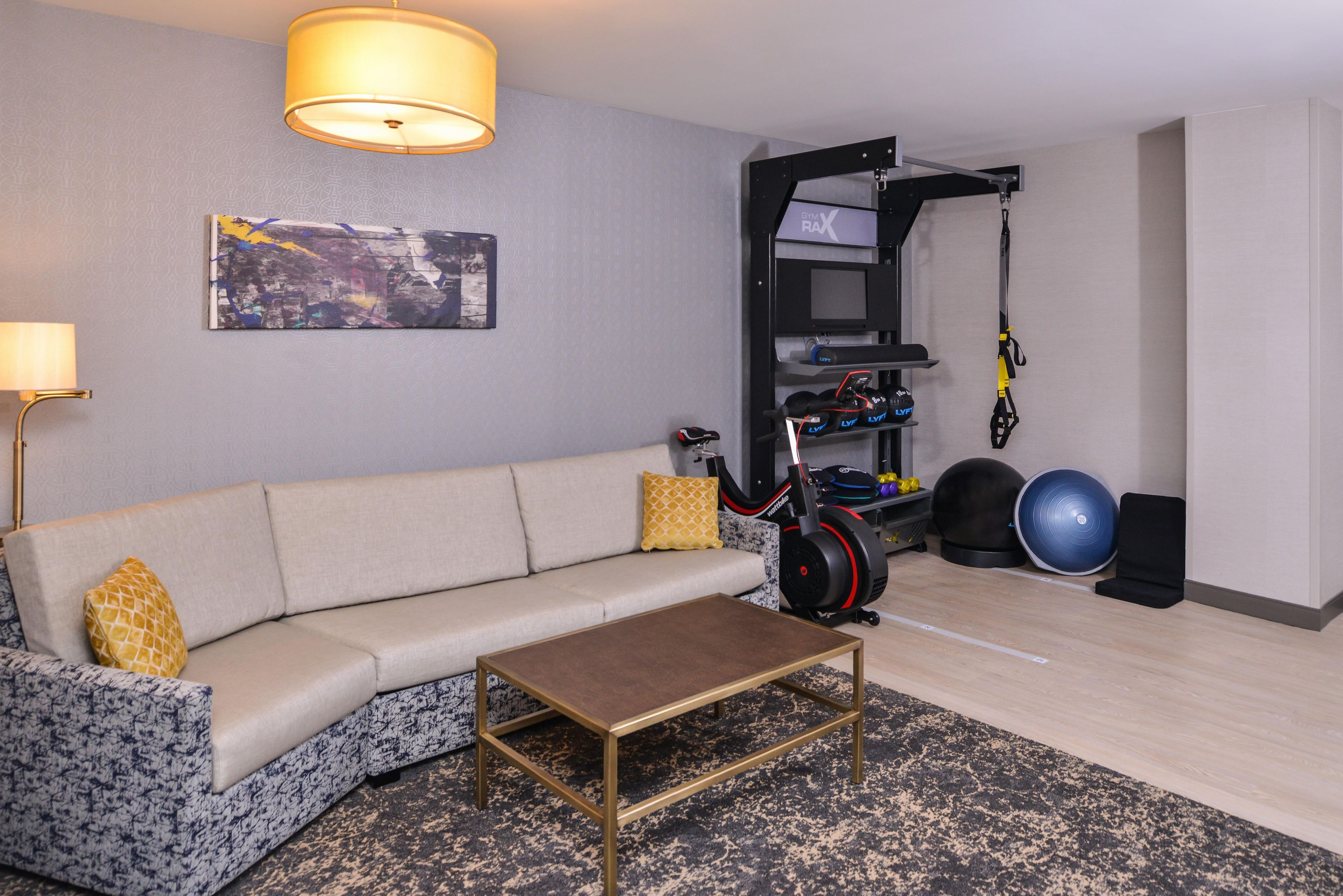 Sala de estar com sofá, mesa de centro, equipamento de exercício fixado na parede e tapete de yoga.