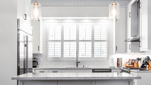 Uma cozinha moderna com armários brancos, uma ilha grande com dois banquetes e iluminação pendente.