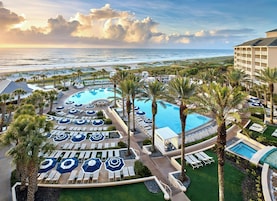 Um resort com uma piscina grande, espreguiçadeiras, palmeiras e vista para o oceano.