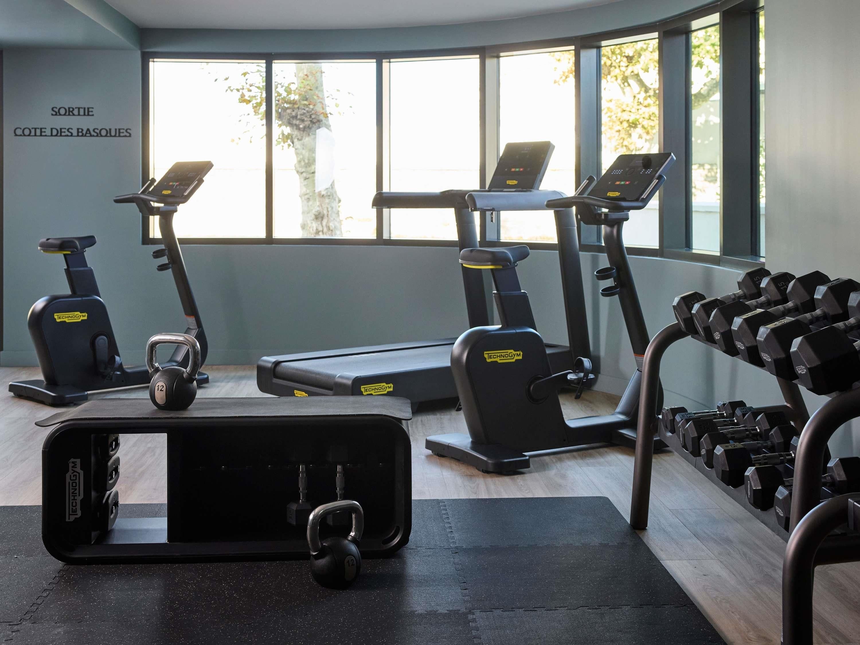 Uma academia com esteiras, um kettlebell e halteres.