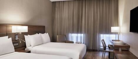 Quarto de hotel com duas camas, uma escrivaninha, uma cadeira e uma televisão.
