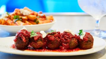 Um prato de almôndegas ao molho de tomate com um enfeite, e uma tigela de massa no fundo.