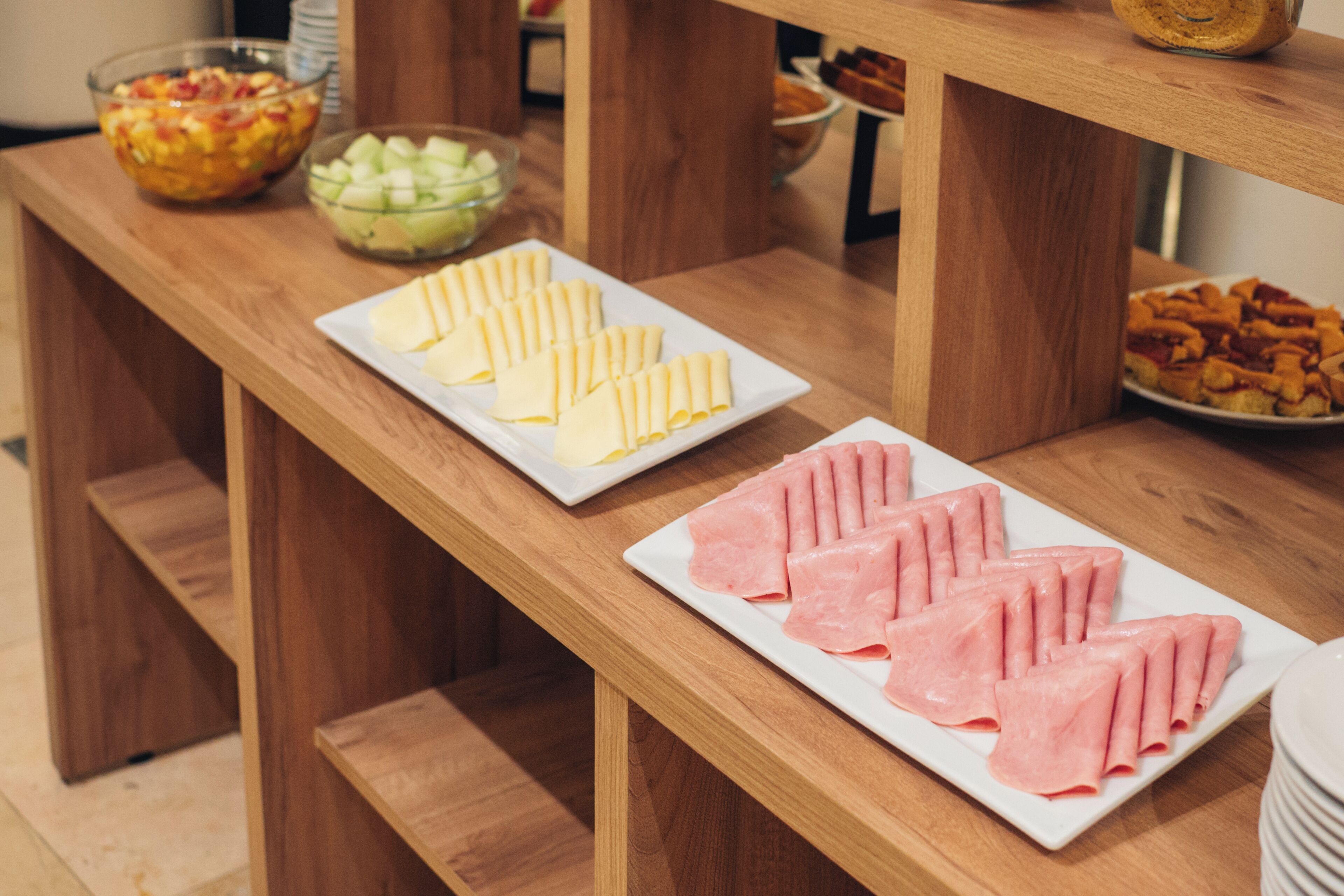 Mesa de buffet com diversos alimentos, incluindo queijo, presunto e frutas.
