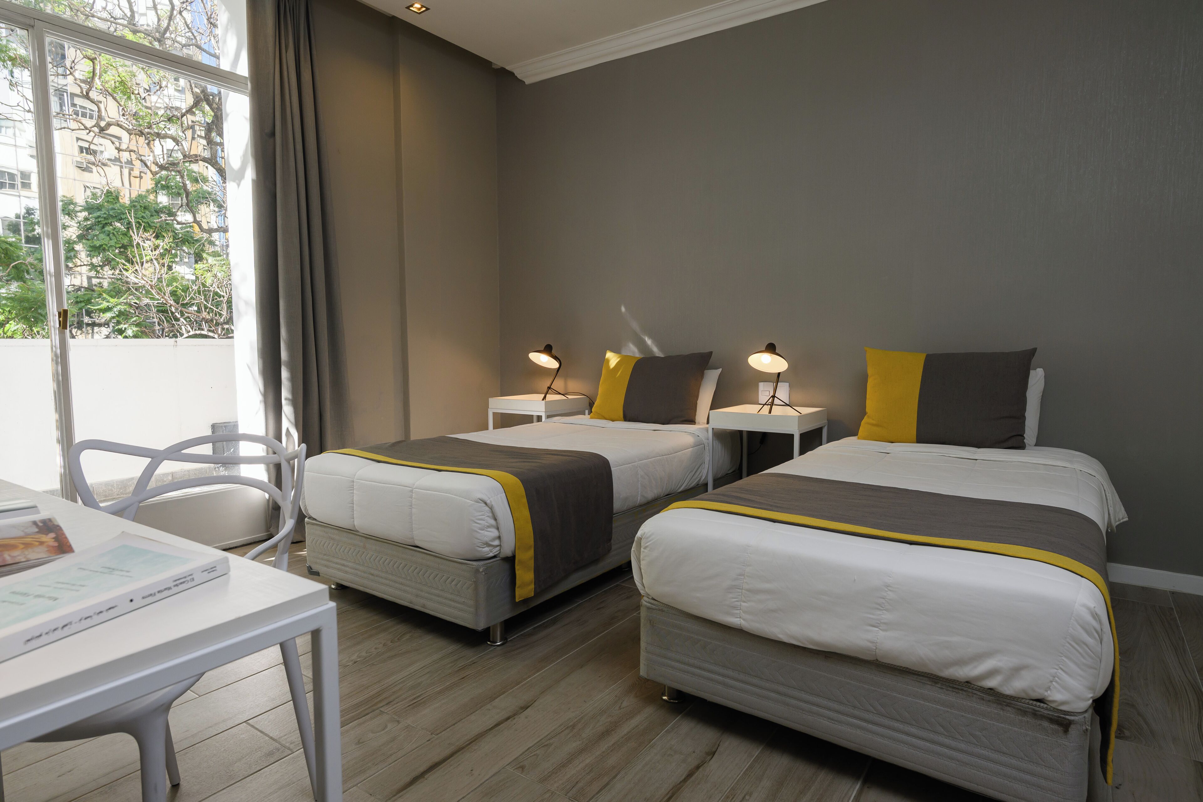 Quarto de hotel com duas camas, uma escrivaninha e uma cadeira.