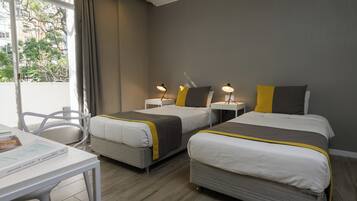 Quarto de hotel com duas camas, uma escrivaninha e uma cadeira.