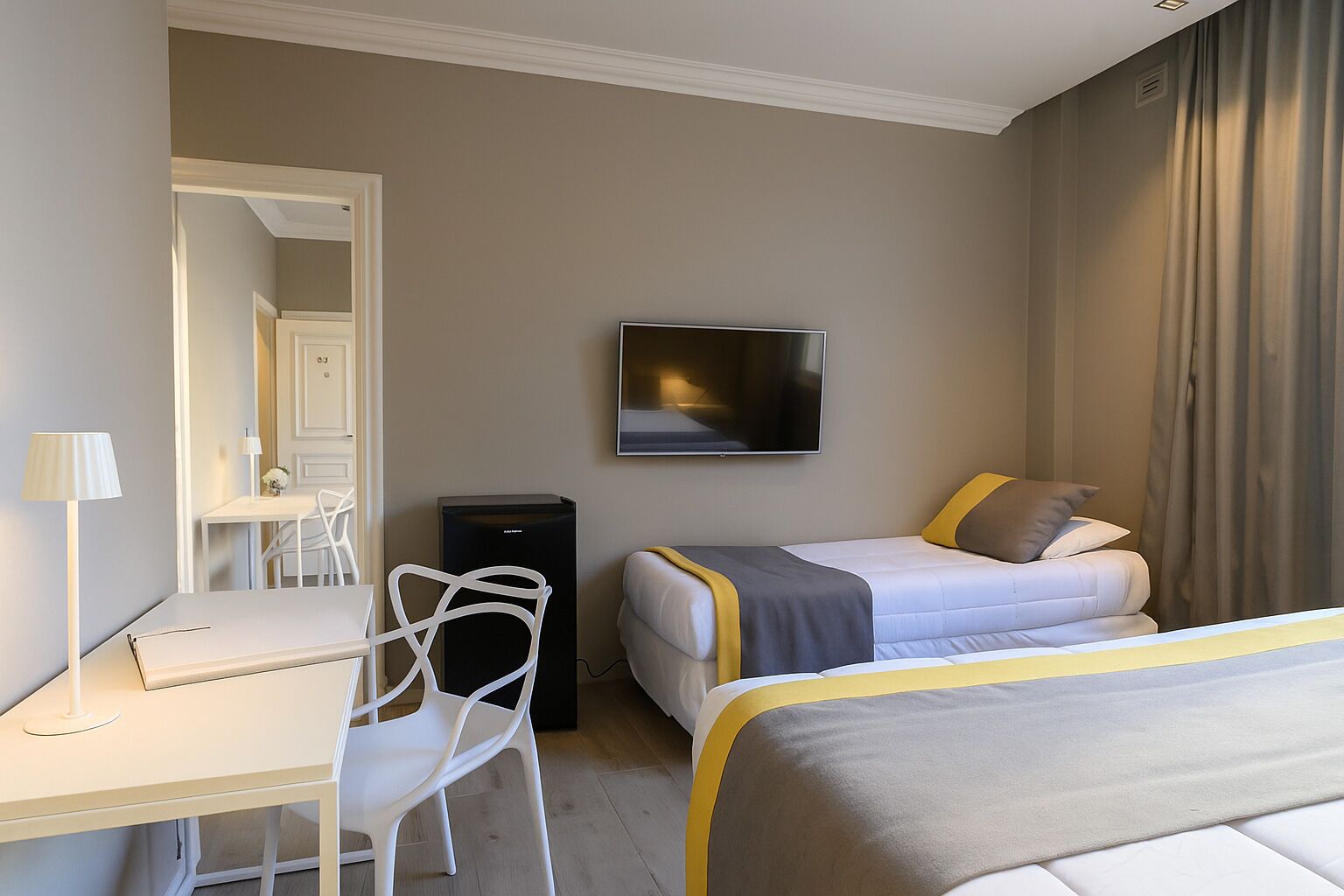 Quarto de hotel com escrivaninha, cadeira, cama, televisão e porta.