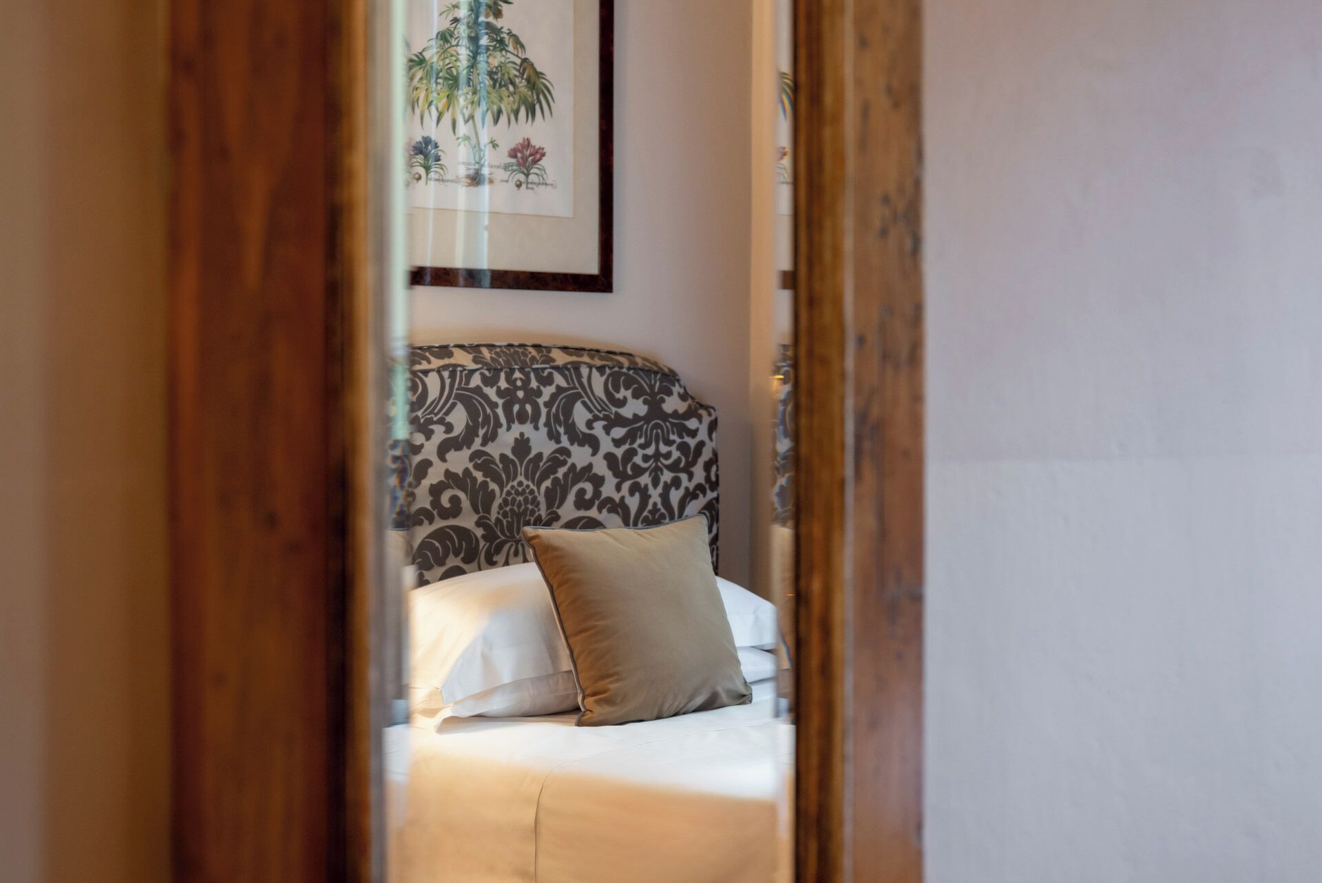 Quarto com uma cama, cabeceira estampada e ilustração botânica emoldurada na parede.