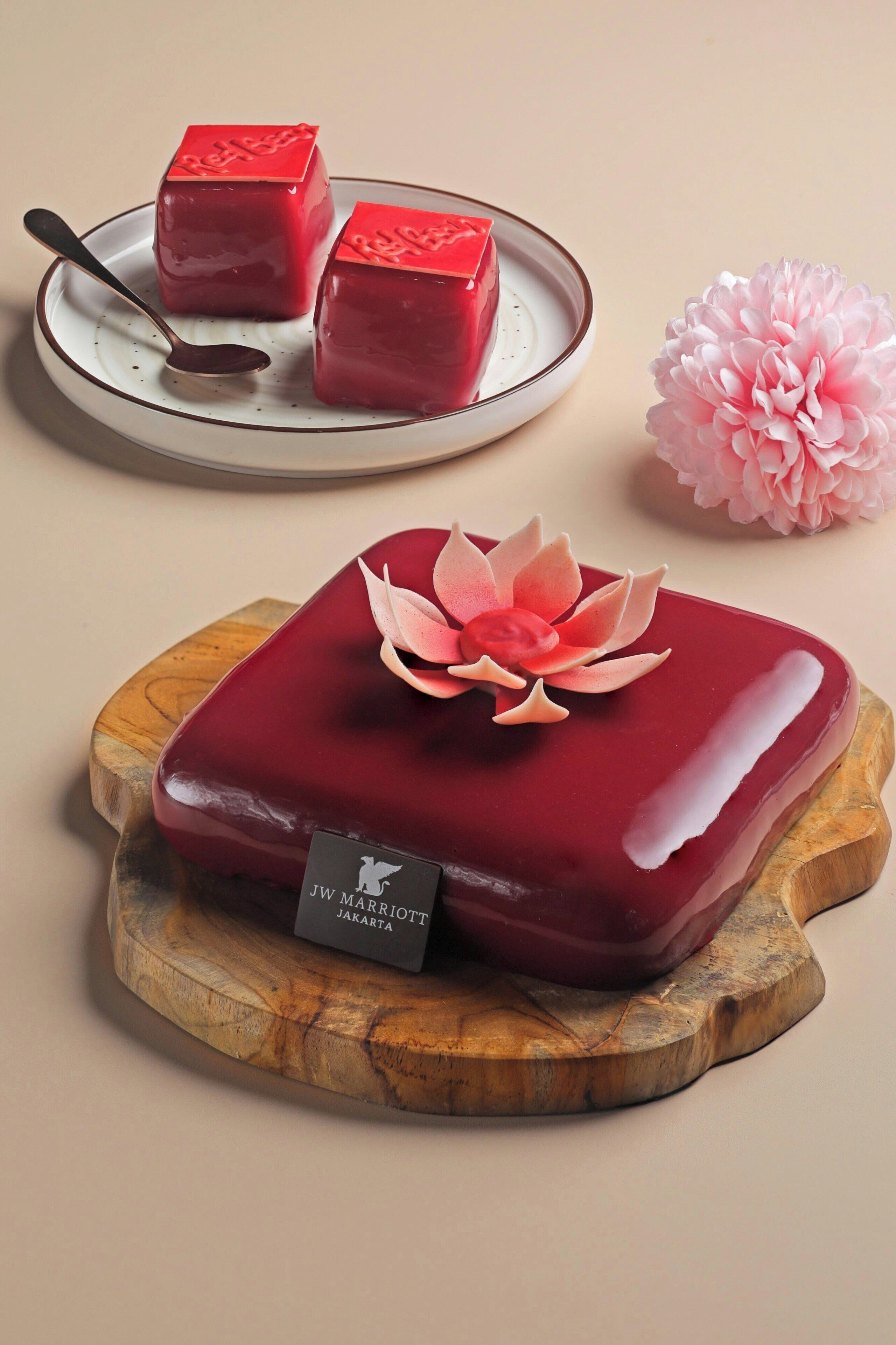 Sobremesa em uma tábua de madeira com etiqueta, um prato com duas sobremesas e uma colher, e uma flor rosa.