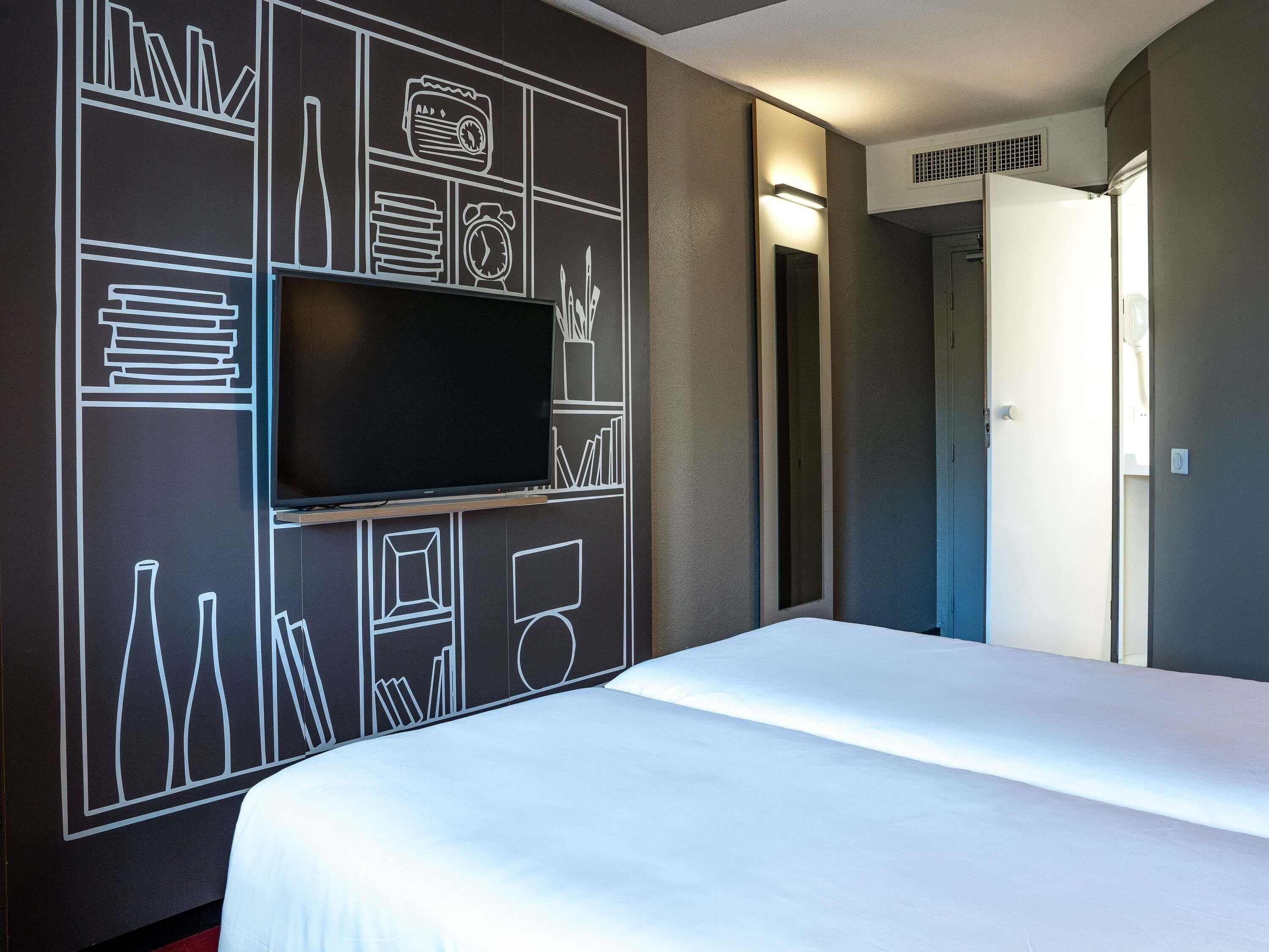 Quarto de hotel com uma cama, uma televisão de tela plana presa à parede e uma porta que dá para outro quarto.