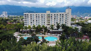 Um hotel com piscina, rodeado por palmeiras e montanhas ao fundo.