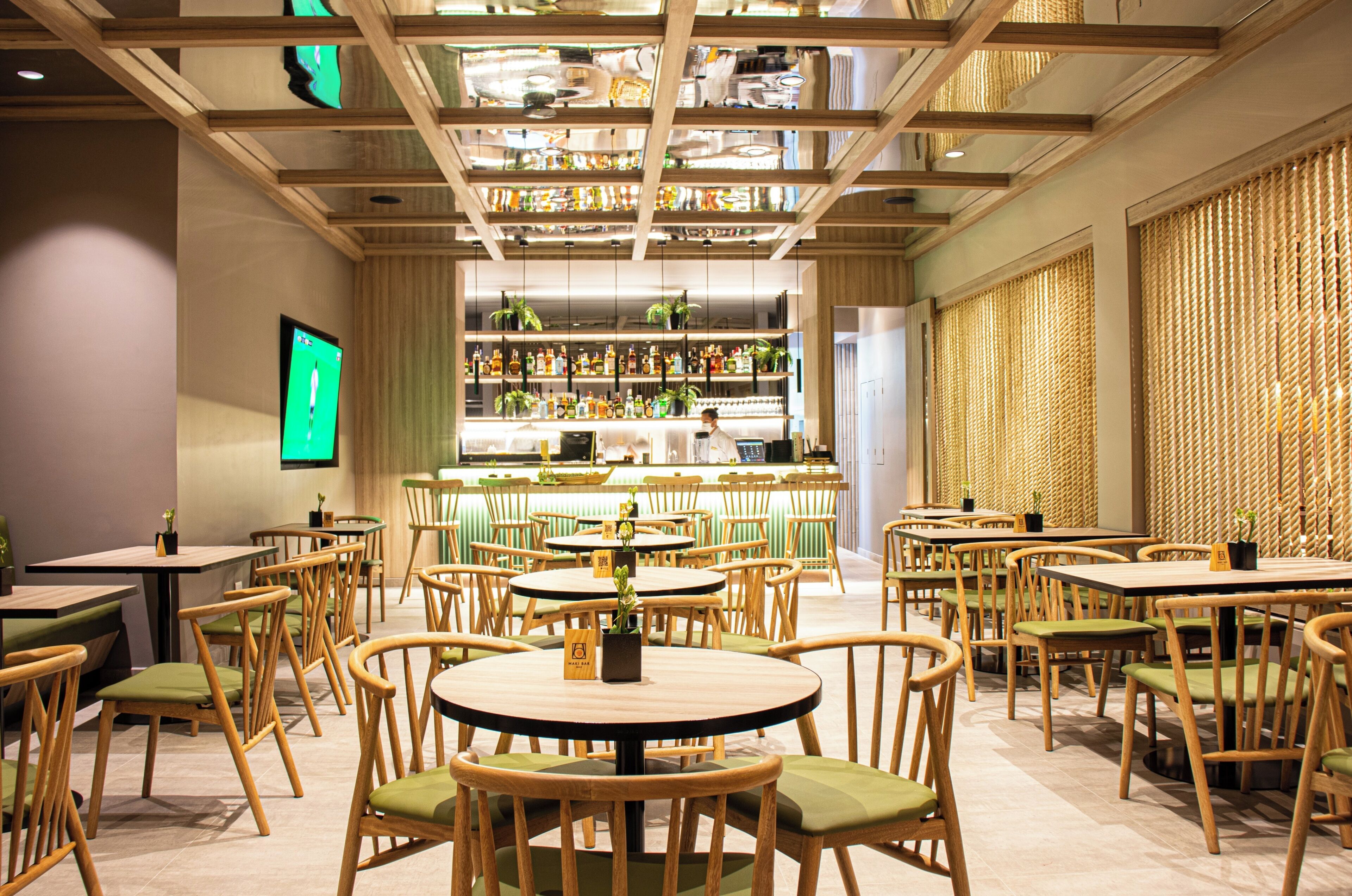 Um restaurante com várias mesas e cadeiras, um espaço de bar e uma placa de saída verde.