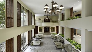 Um amplo átrio com vários níveis, pé-direito alto, escadaria central e um lustre.