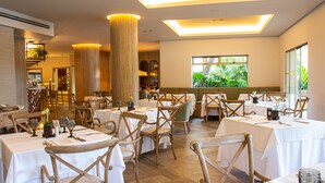Um restaurante com toalhas de mesa brancas, cadeiras de madeira e grandes janelas que dão para o verde.