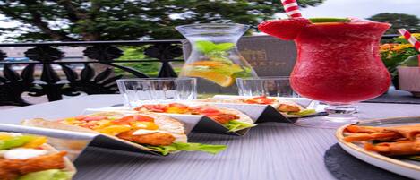 Uma mesa com comida e bebidas, incluindo tacos, um jarro e um coquetel com canudo.
