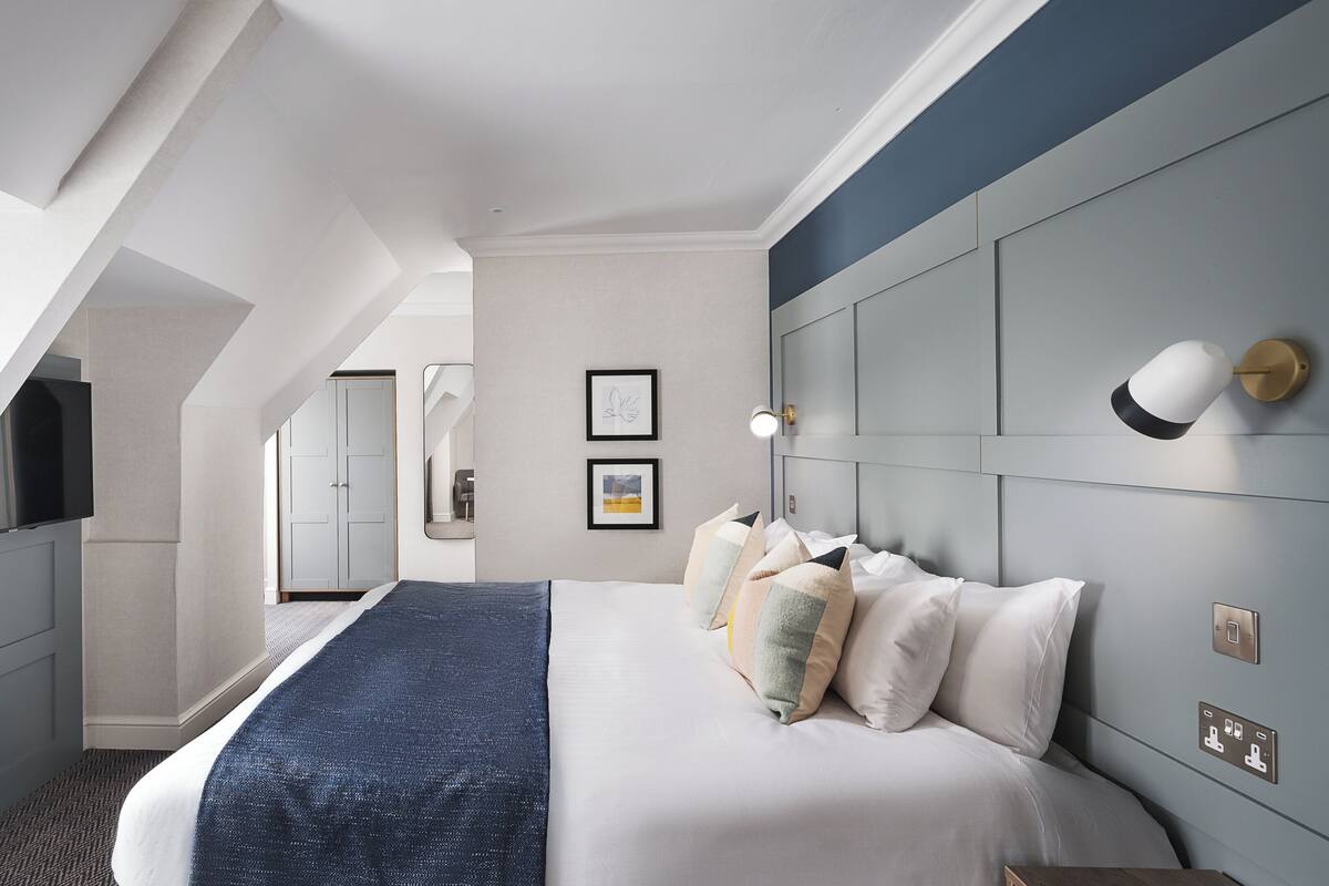 Quarto de hotel moderno com uma cama grande, televisão de tela plana, escrivaninha e uma cadeira.