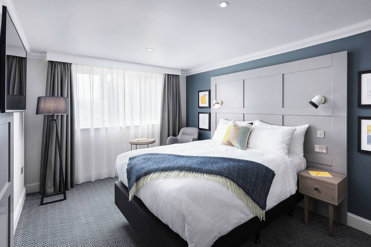 Quarto de hotel moderno com uma cama grande, uma mesa de cabeceira, uma cadeira e uma escrivaninha.