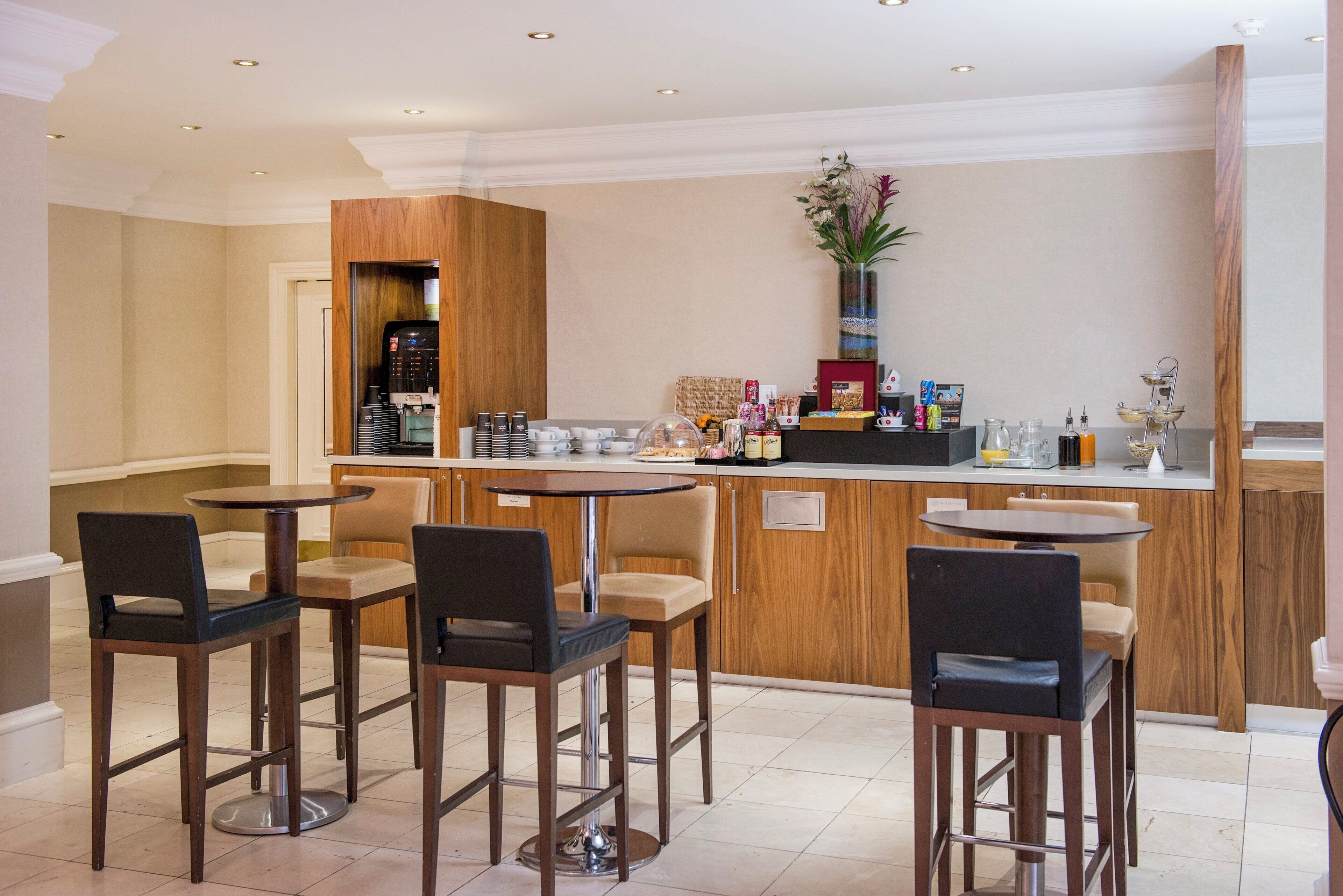 Uma área de bar com uma máquina de café, banquetas e um balcão com diversos itens.