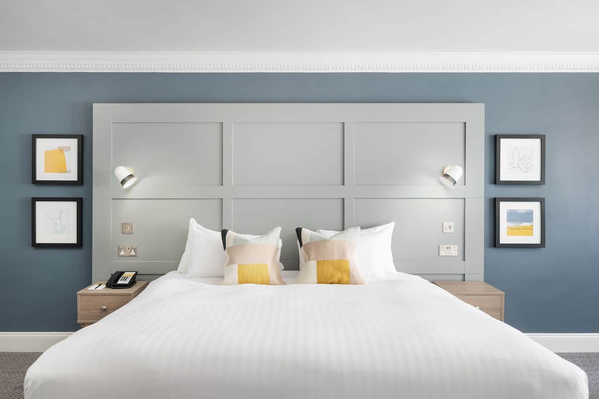 Quarto de hotel com uma cama grande, duas mesas de cabeceira e uma cabeceira com iluminação embutida.