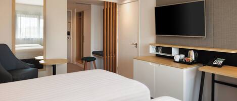 Quarto de hotel com uma cama, uma escrivaninha com televisão de tela plana, cafeteira e telefone.