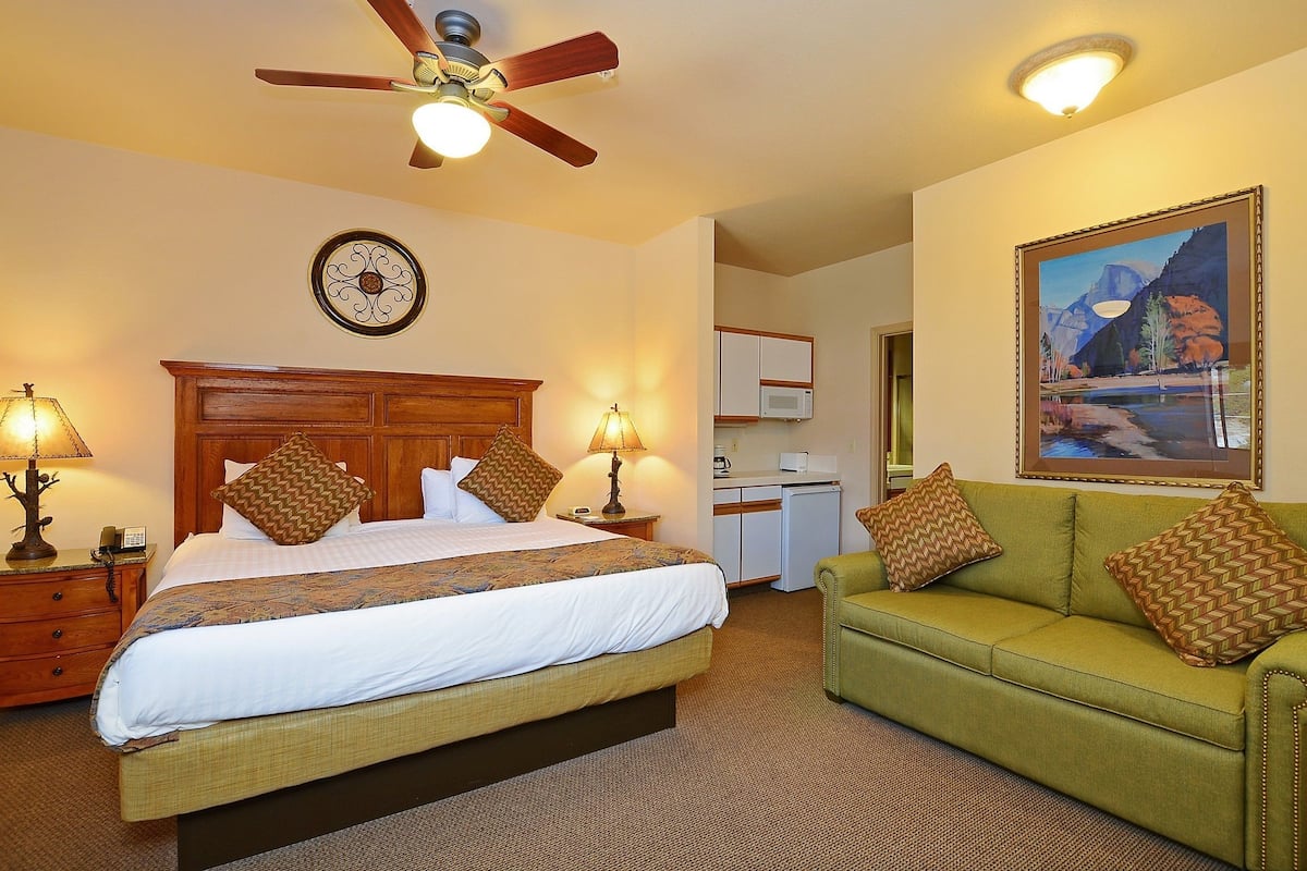 Quarto de hotel com uma cama grande, um sofá verde, um ventilador de teto e um quadro na parede.
