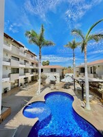 Uma área de piscina com piscina azul, cadeiras de descanso e palmeiras.