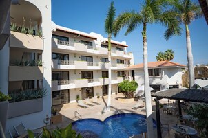 Um hotel com piscina, várias varandas e palmeiras.