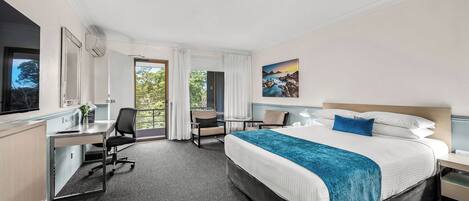 Quarto de hotel com cama, escrivaninha, cadeira e vista para o exterior.