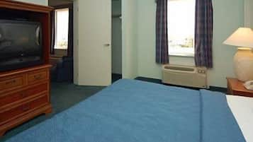 Quarto de hotel com cama, televisão em cómoda de madeira, janela com cortinas e abajur numa mesinha de cabeceira.