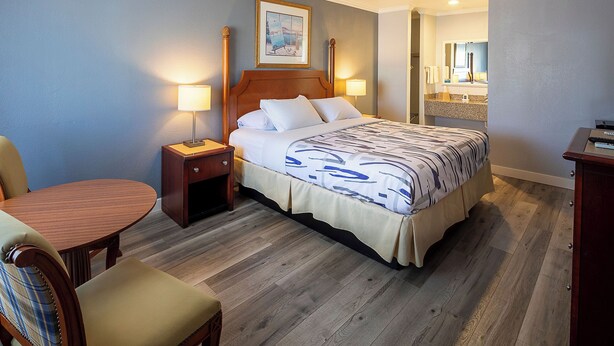 Quarto de hotel com cama, mesas de cabeceira, uma cadeira e uma escrivaninha.