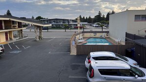 Um estacionamento com piscina, um carro branco e um edifício com varanda.