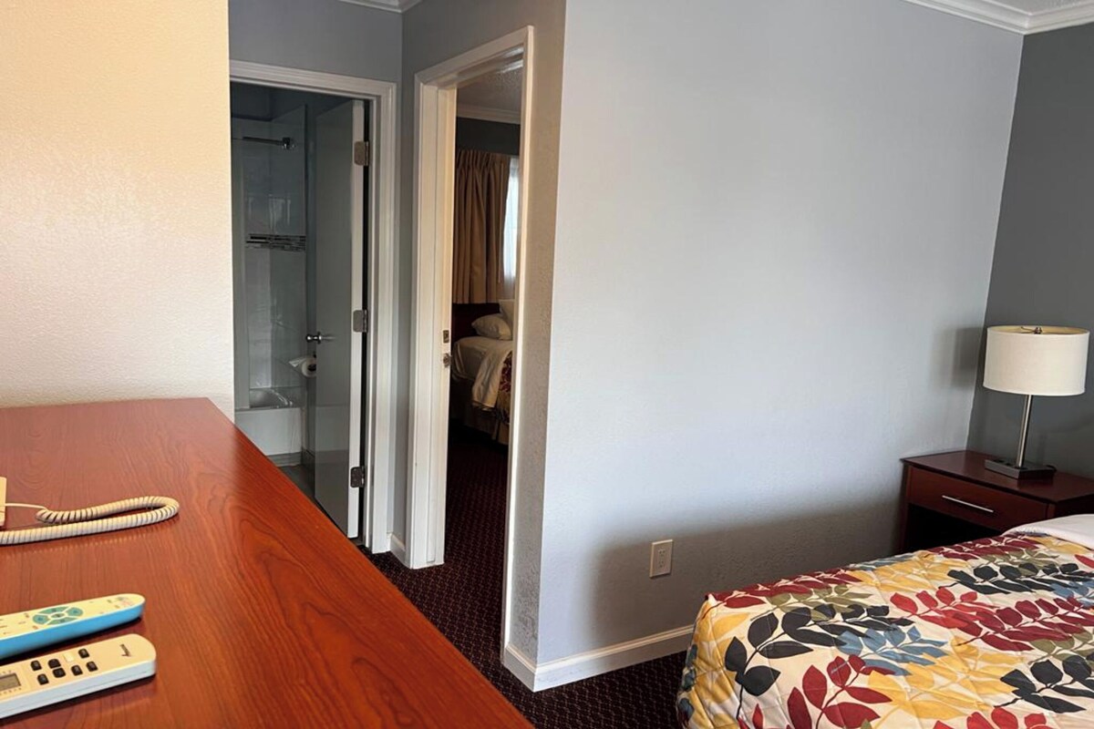 Quarto de hotel com escrivaninha de madeira, cama com colcha estampada em flores e vista para o banheiro.