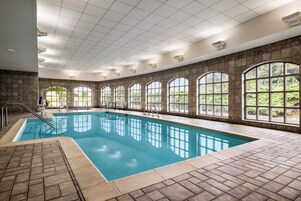 Piscina interior com paredes de pedra e amplas janelas em arco.