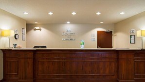 Uma mesa de recepção com acabamento em madeira, um relógio e uma placa indicando ser uma Quality Inn da Choice Hotels.