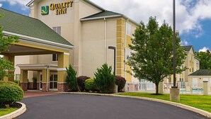 Um hotel Quality Inn com entrada coberta, estacionamento e área ajardinada com árvores.