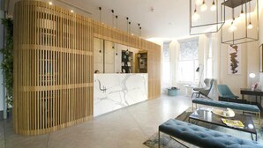 Um lobby de hotel moderno com um balcão de recepção de madeira, área de estar com um sofá e poltronas, e uma parede de destaque em mármore.