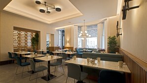 Interior de restaurante moderno com pé direito alto, iluminação pendente e uma combinação de mesas e cabines.