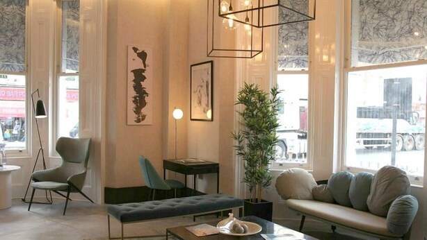 Uma sala de estar moderna com sofá, poltrona e banco, uma planta em vaso e obras de arte nas paredes.