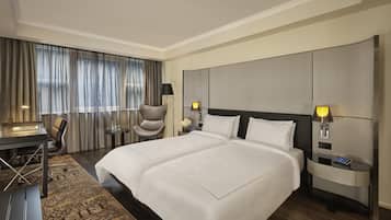 Quarto de hotel com uma cama grande, uma escrivaninha, uma cadeira, uma mesinha de cabeceira e uma luminária.