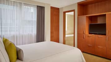 Quarto de hotel com uma cama, uma televisão sobre um móvel de madeira e uma porta de banheiro.