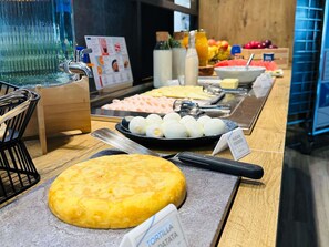 Um buffet de café da manhã com diversos alimentos, incluindo tortillas, ovos e uma variedade de frutas e vegetais.