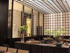 Interior de restaurante com teto em padrão quadriculado, painéis de madeira e plantas em vasos no balcão.
