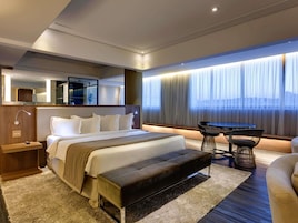Quarto de hotel moderno com cama grande, mesas de cabeceira, escrivaninha e uma cadeira.