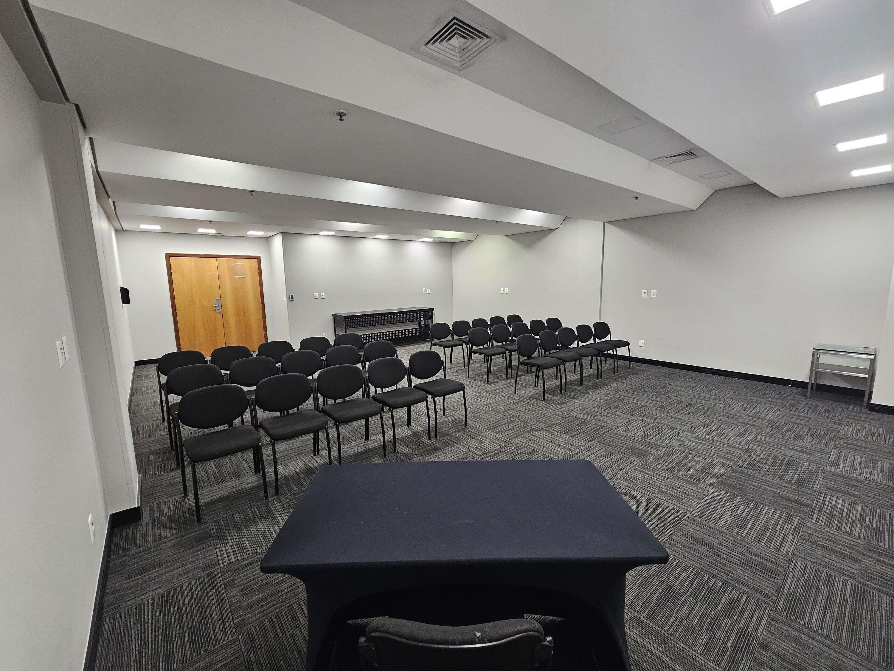 Uma sala de conferências com fileiras de cadeiras, um pódio e piso coberto de carpete.