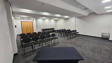 Uma sala de conferências com fileiras de cadeiras, um pódio e piso coberto de carpete.