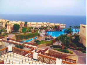 Um resort com uma grande piscina, palmeiras e vista para o oceano.