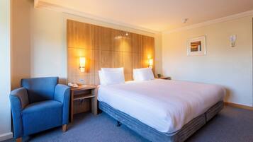 Quarto de hotel com uma cama grande, uma cadeira, mesa de cabeceira com telefone e duas luminárias fixadas na parede.