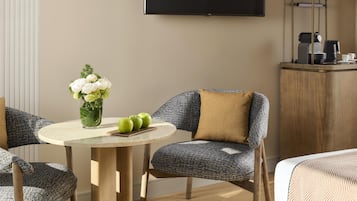 Quarto de hotel com mesa redonda, duas cadeiras, um vaso com flores e um cantinho para café.
