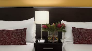 Quarto de hotel com duas camas, uma mesa de cabeceira com abajur e um vaso com flores.
